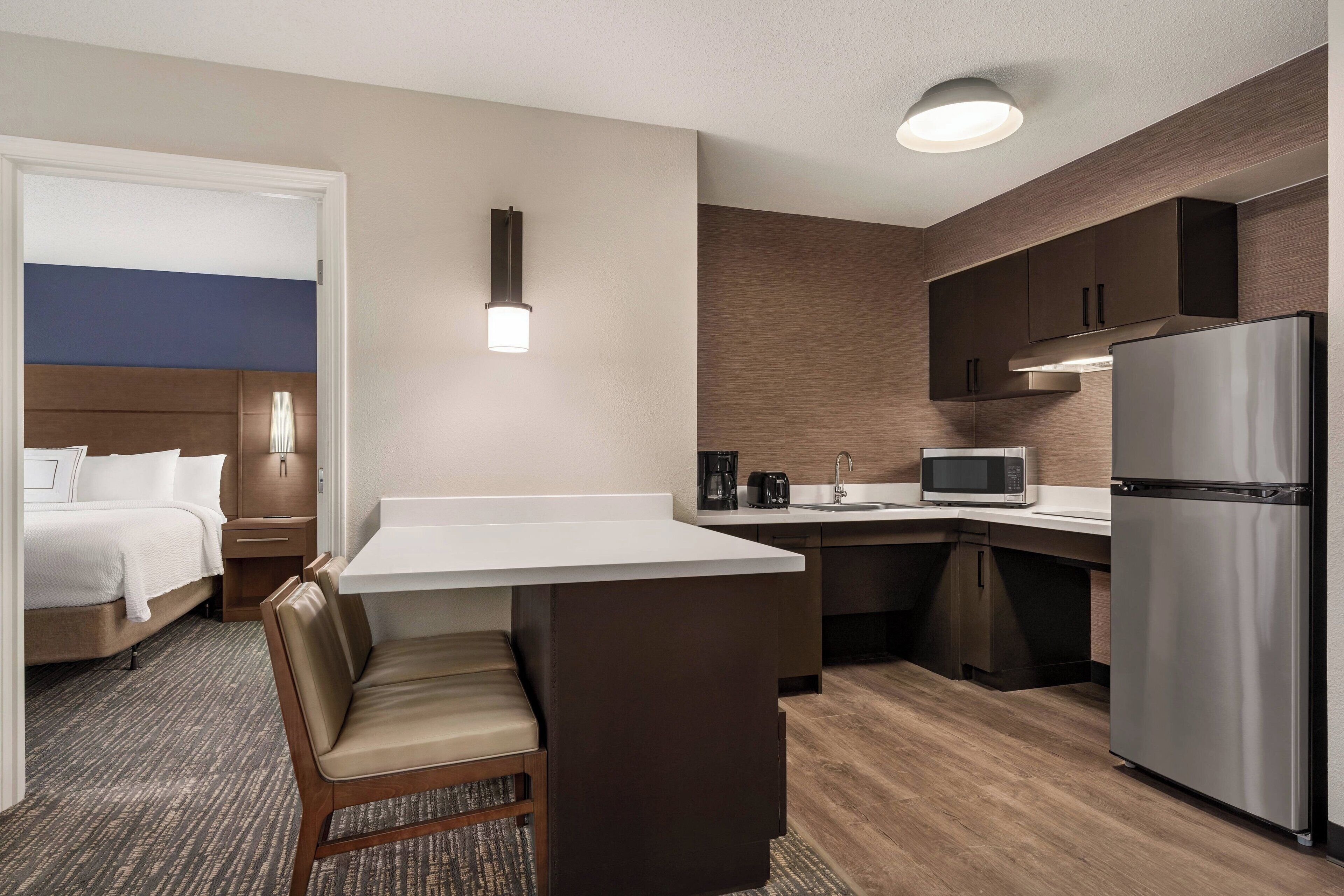 Quarto de hotel pequeno com cozinha compacta, uma cama, área de estar e banheiro.