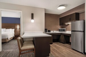 Quarto de hotel pequeno com cozinha compacta, uma cama, área de estar e banheiro.