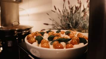 Uma tigela branca cheia de tomates cereja e folhas de manjericão em uma bancada de cozinha.