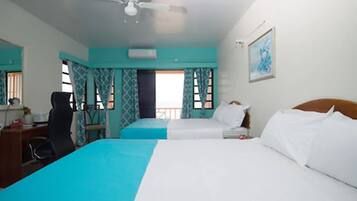 Quarto de hotel com duas camas, uma escrivaninha, uma cadeira e um ventilador de teto.