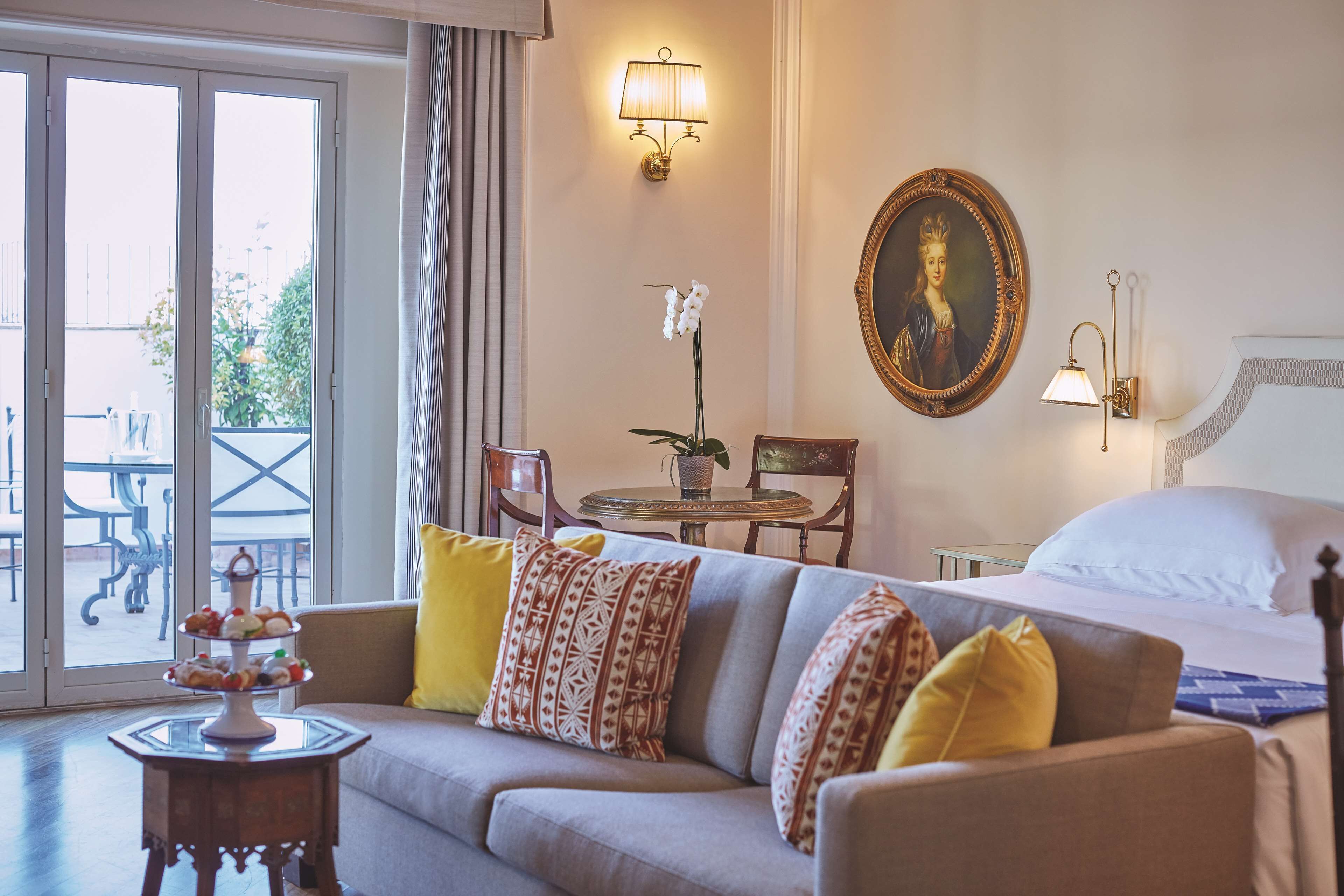 Quarto de hotel com sofá, mesa de jantar com um vaso, cama e um quadro na parede.