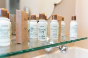 Uma prateleira de banheiro com diversos produtos Aveda, incluindo uma caixa e várias garrafas de shampoo.