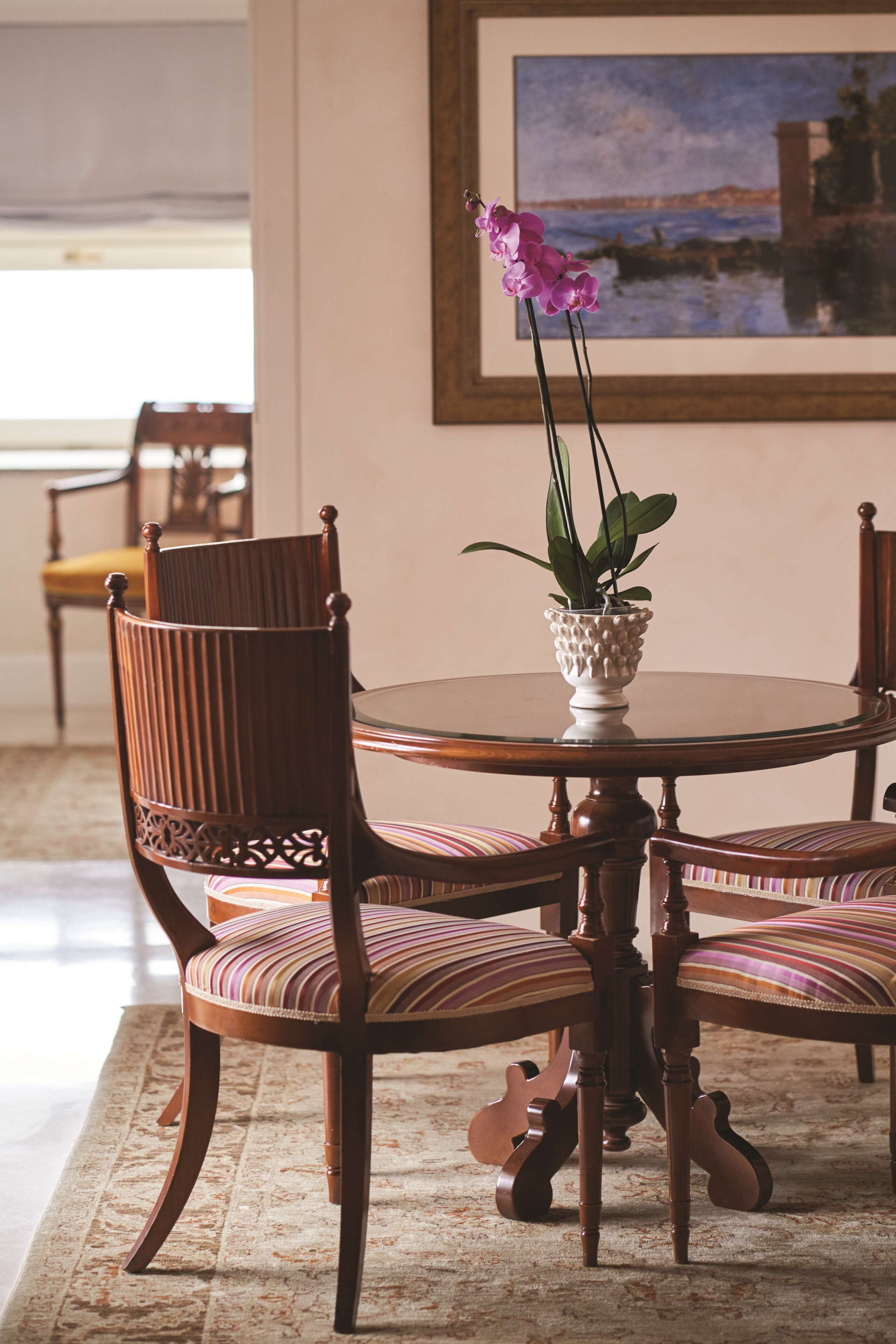 Uma sala de jantar com mesa redonda, cadeiras e um vaso com flores.