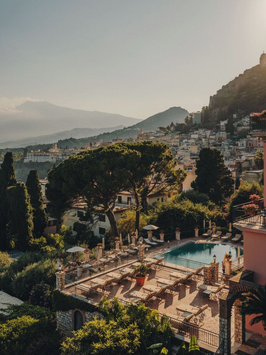 Uma área à beira da piscina com espreguiçadeiras, piscina e vista para uma vila na colina.