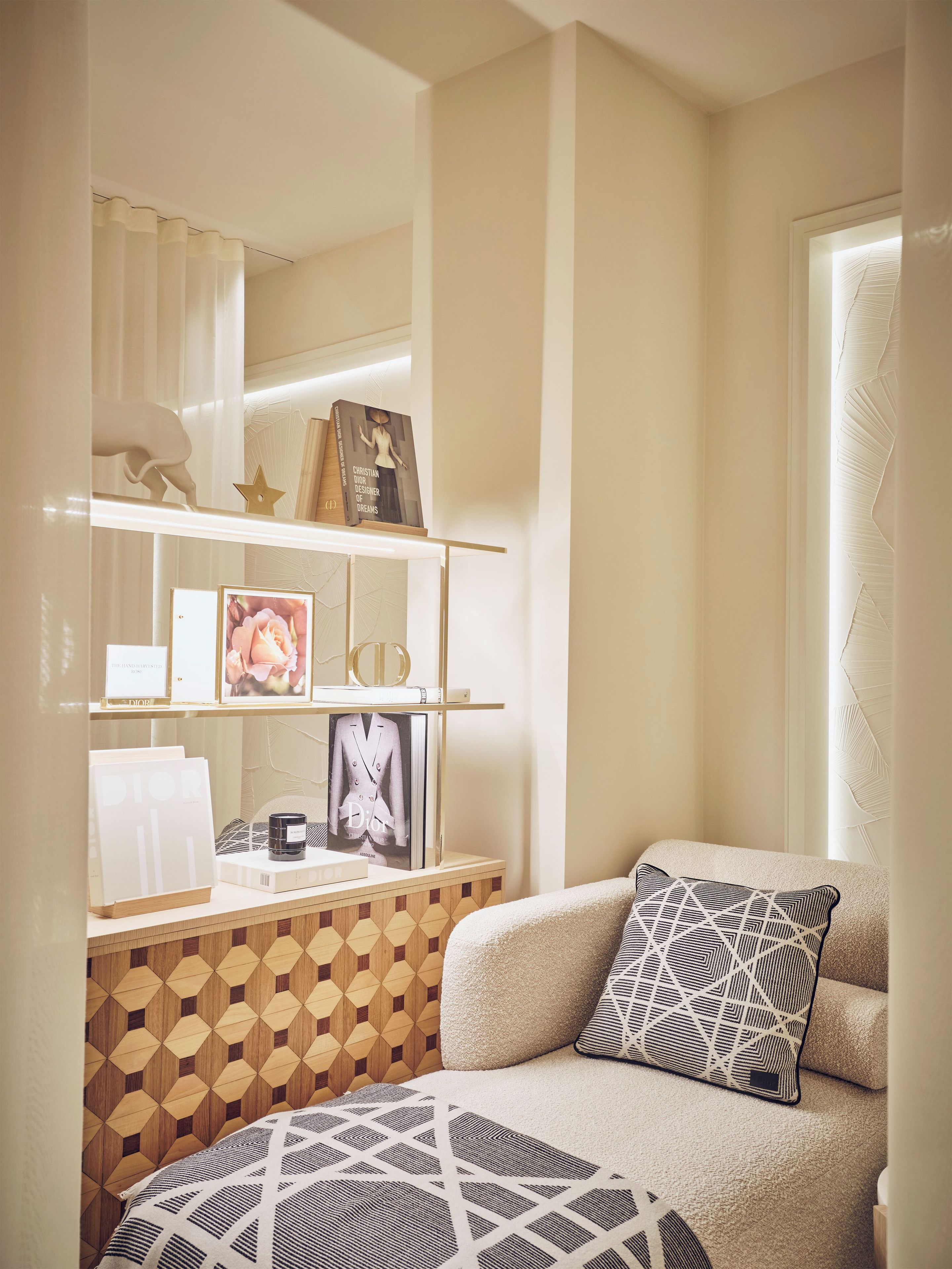 Quarto com uma cama, uma estante com livros e objetos decorativos, e uma parede com padrão geométrico.