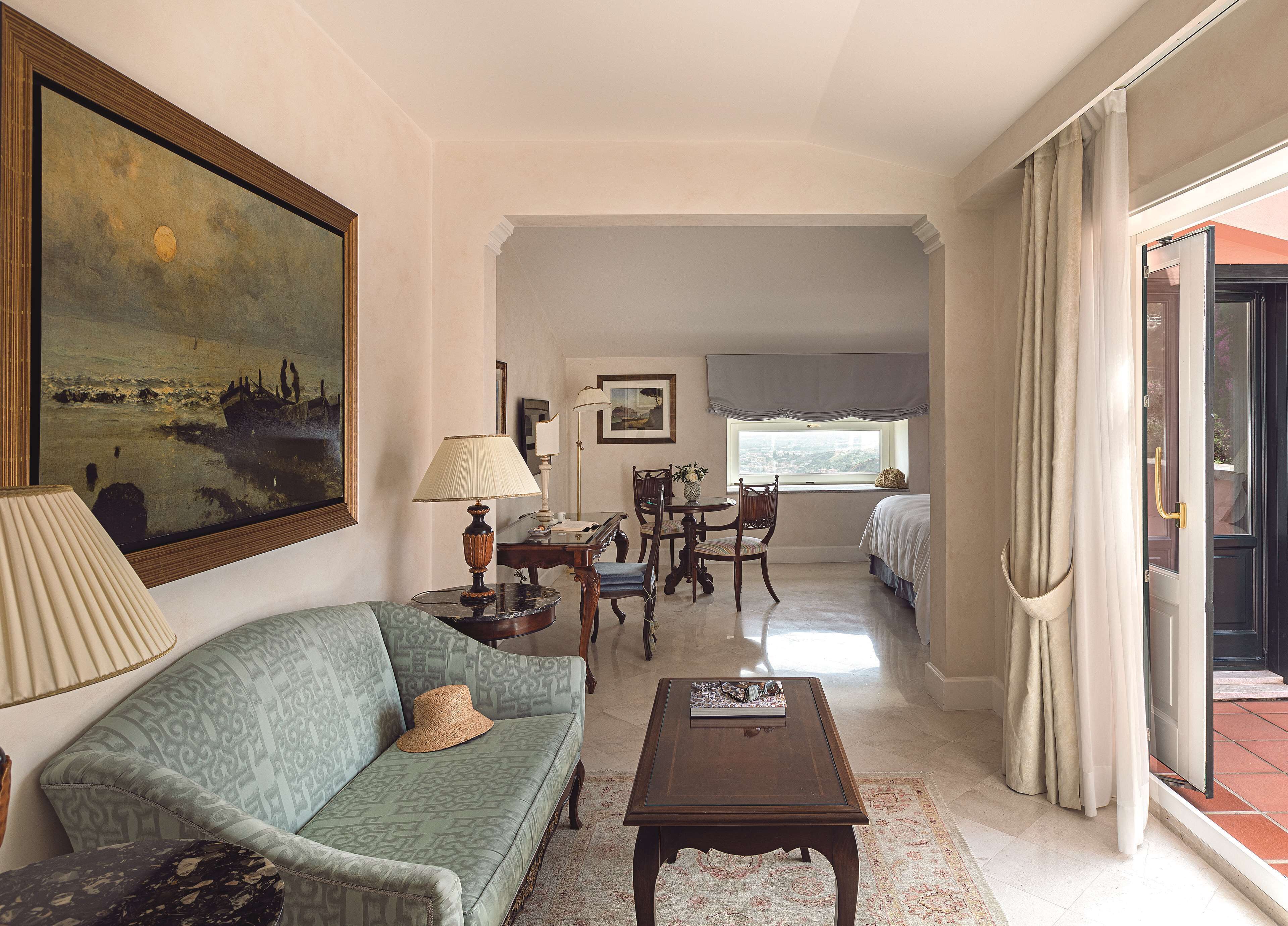 Uma sala de estar com sofá, mesa de centro, quadro, luminária, mesa de jantar com cadeiras e janela com cortinas.