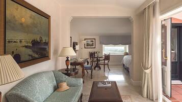 Uma sala de estar com sofá, mesa de centro, quadro, luminária, mesa de jantar com cadeiras e janela com cortinas.