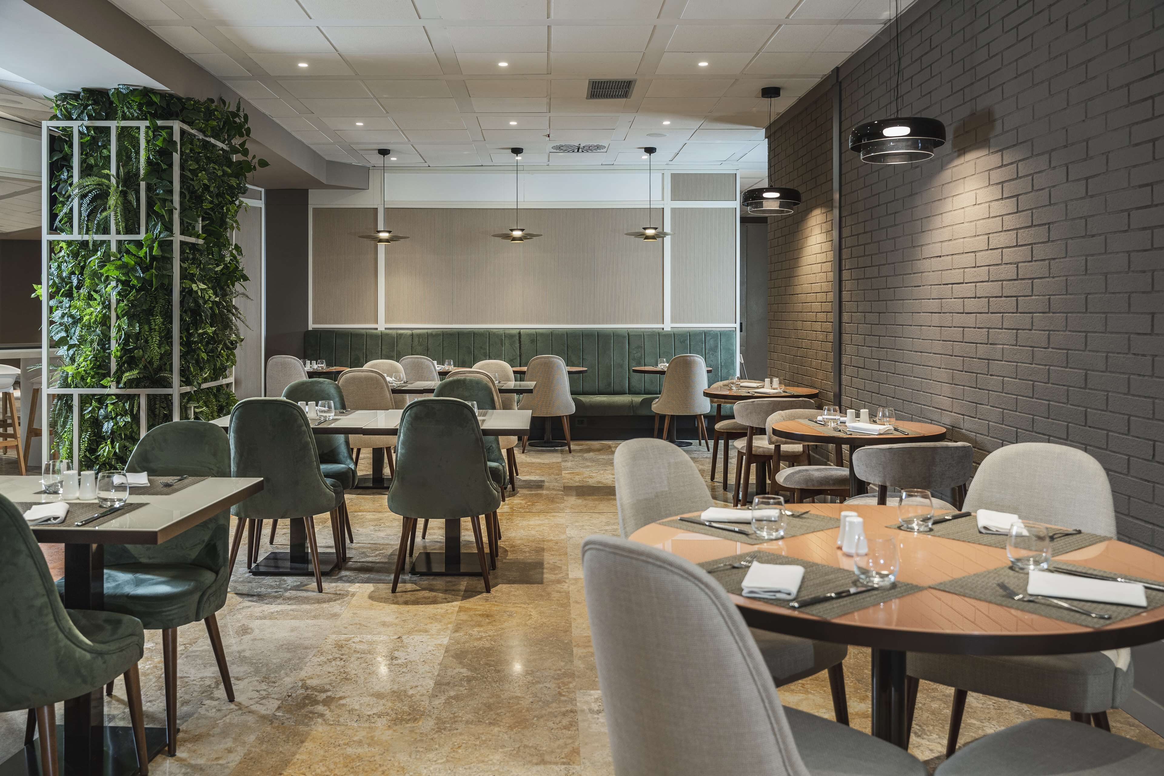 Restaurante moderno com parede verde, várias áreas de estar e iluminação pendente.