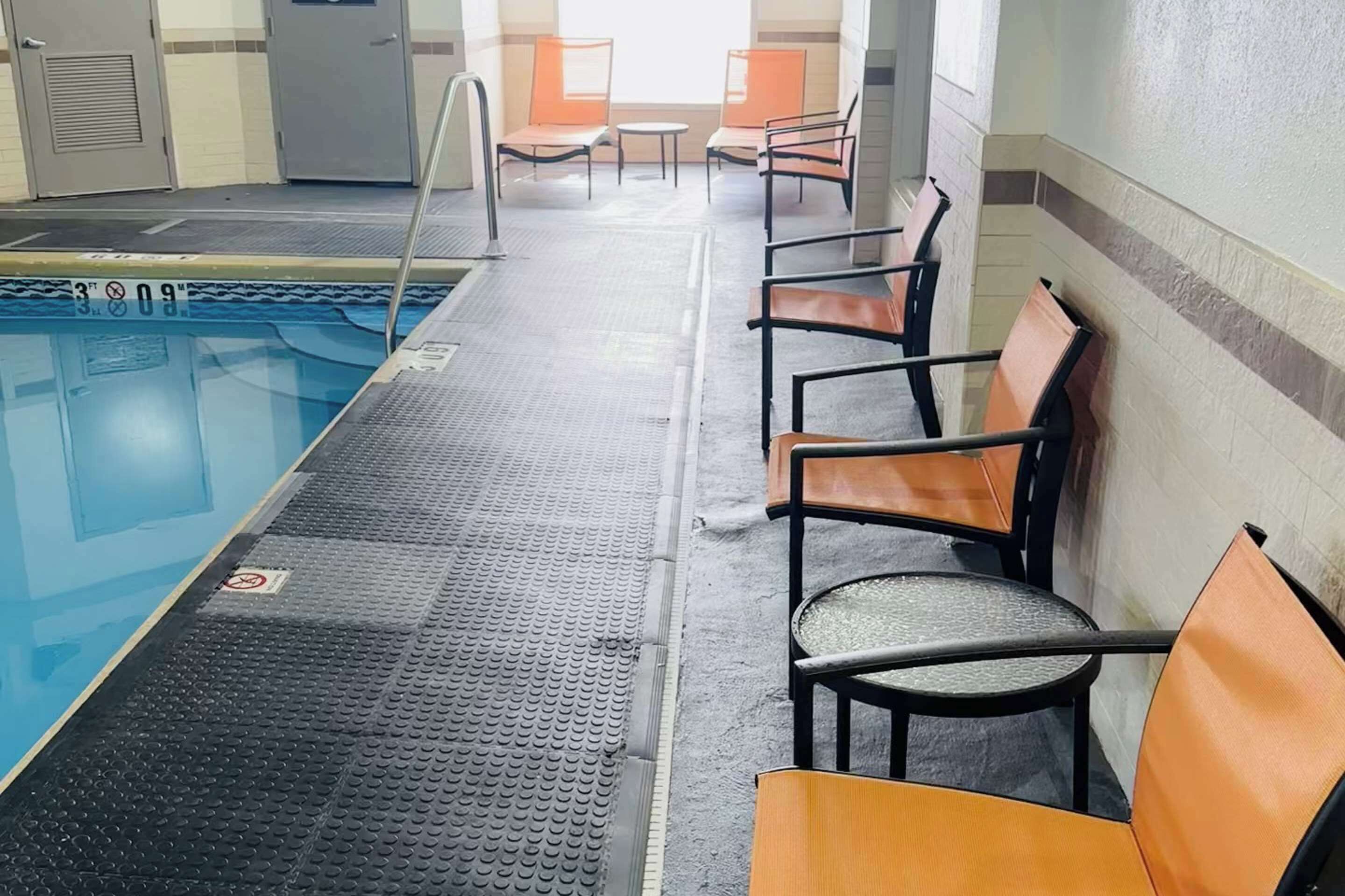Área de piscina com trampolim, cadeiras de espreguiçadeira e um caminho de azulejos.