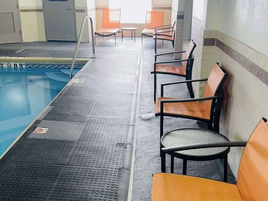 Área de piscina com trampolim, cadeiras de espreguiçadeira e um caminho de azulejos.