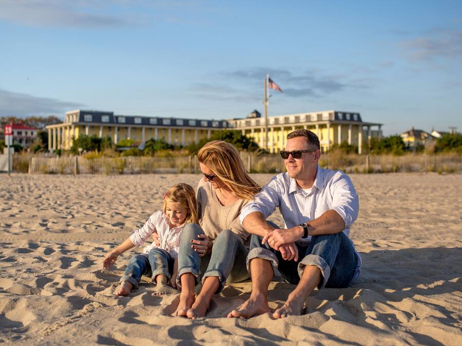 Uma família numa praia de areia, com um edifício grande ao fundo.