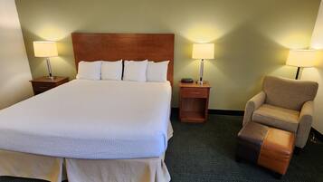 Quarto de hotel com uma cama grande, duas mesas de cabeceira com luminárias, uma cadeira e piso coberto por carpete.