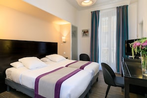 Quarto de hotel com duas camas, uma escrivaninha, uma cadeira, uma televisão e uma janela com cortinas.