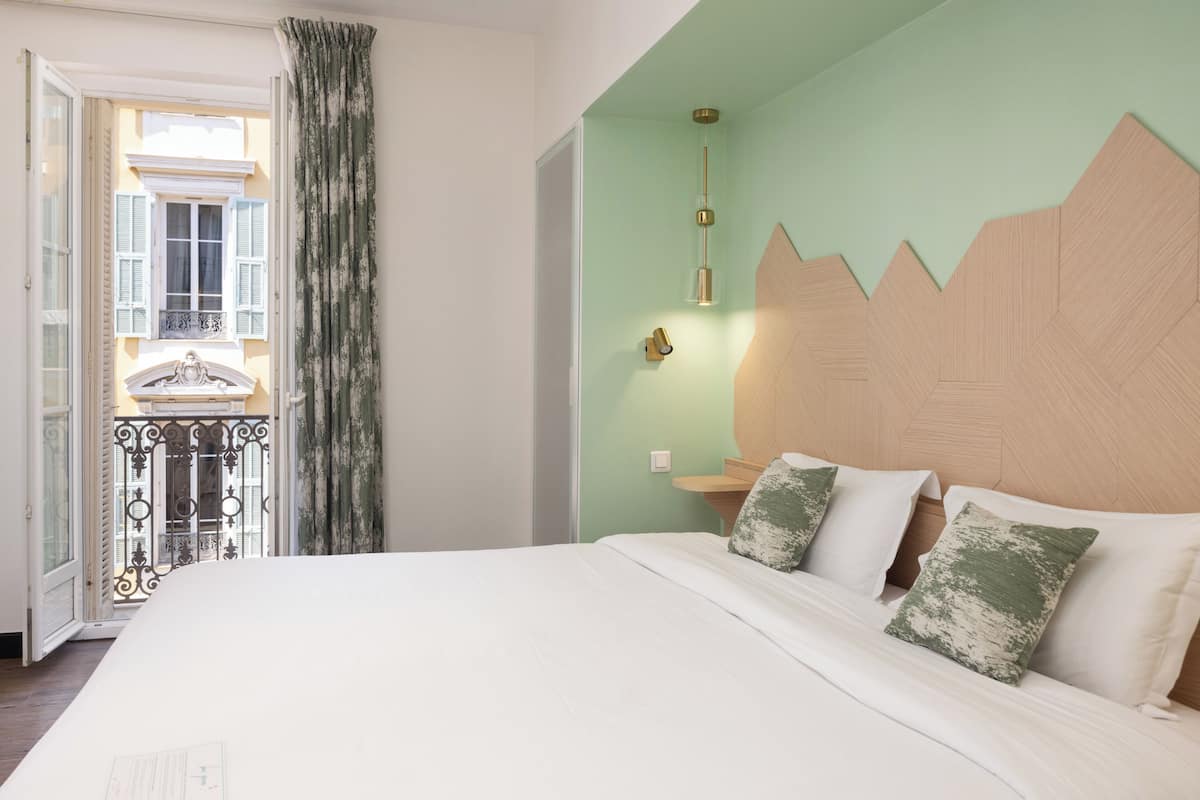 Quarto com uma cama grande, cabeceira de madeira, mesa de cabeceira e janela com persianas.