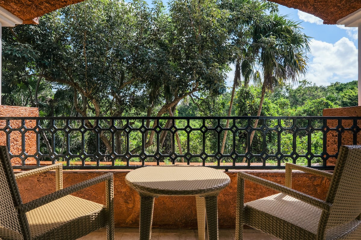 Varanda com móveis de vime, vista para vegetação exuberante e céu claro.