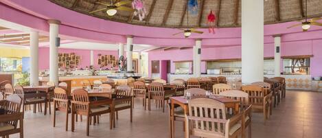 Uma sala de jantar ampla com mesas e cadeiras de madeira, telhado de palha e paredes cor-de-rosa.