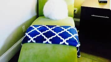 Quarto pequeno com uma cama de solteiro, roupa de cama estampada, travesseiro branco e mesa de cabeceira com abajur.