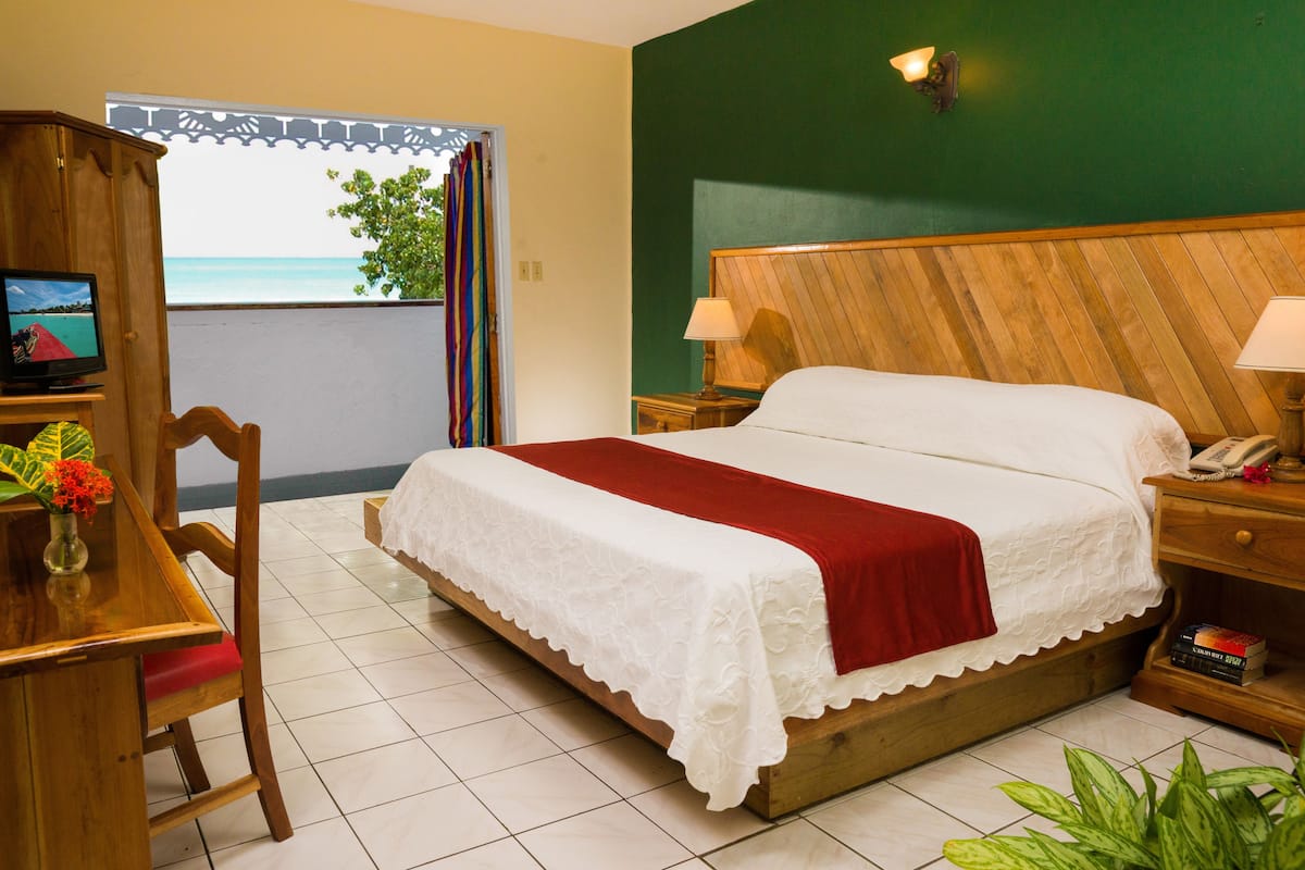 Quarto de hotel com cama, escrivaninha com televisão, cadeira, janela com vista para o oceano e uma planta.