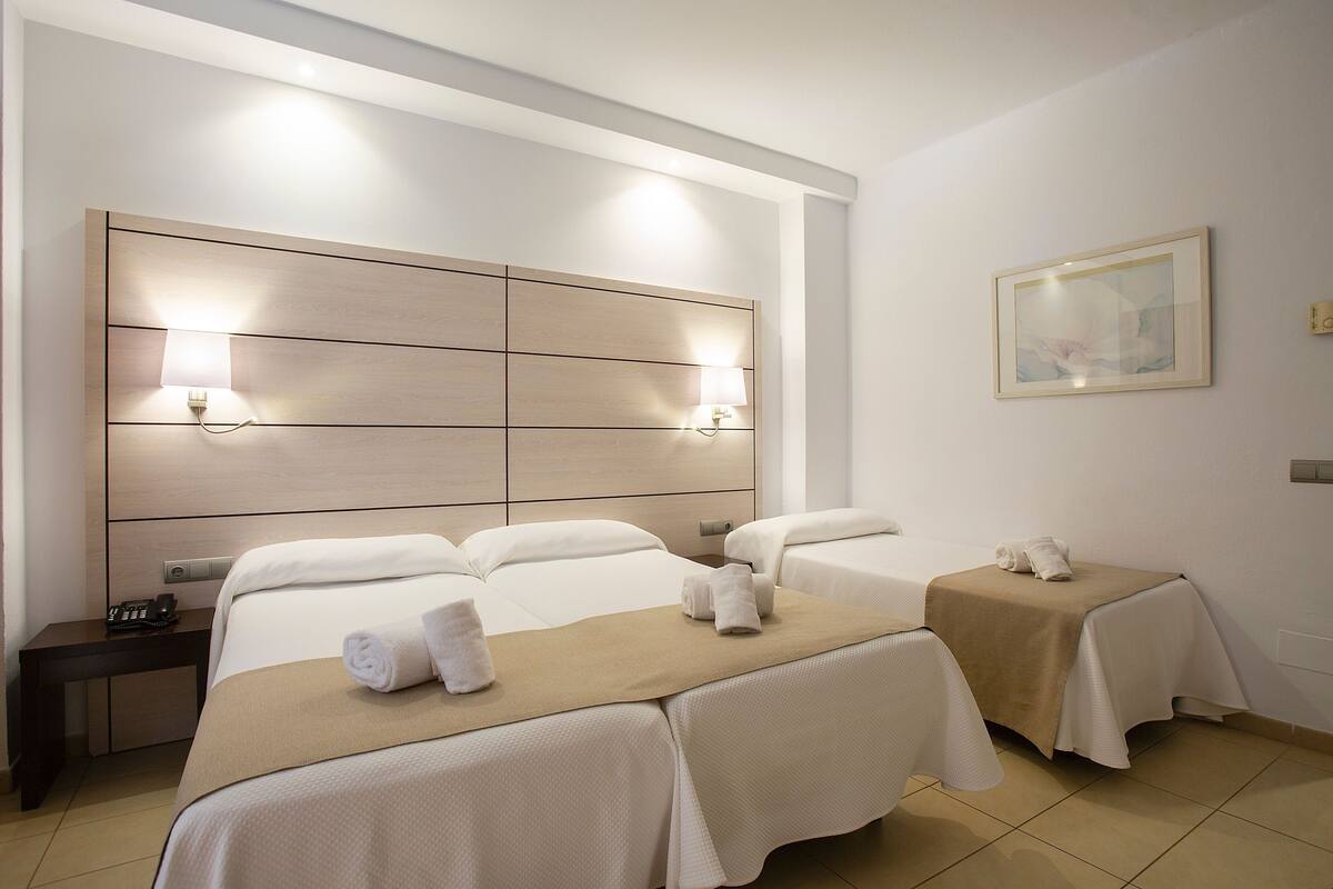 Quarto de hotel com duas camas, uma mesinha de cabeceira e um quadro na parede.