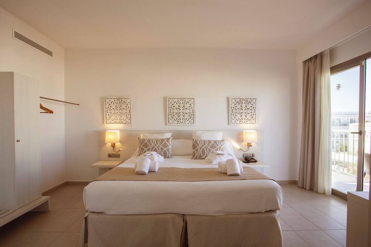 Quarto de hotel com uma cama grande, duas mesas de cabeceira, decoração na parede e vista para o exterior.