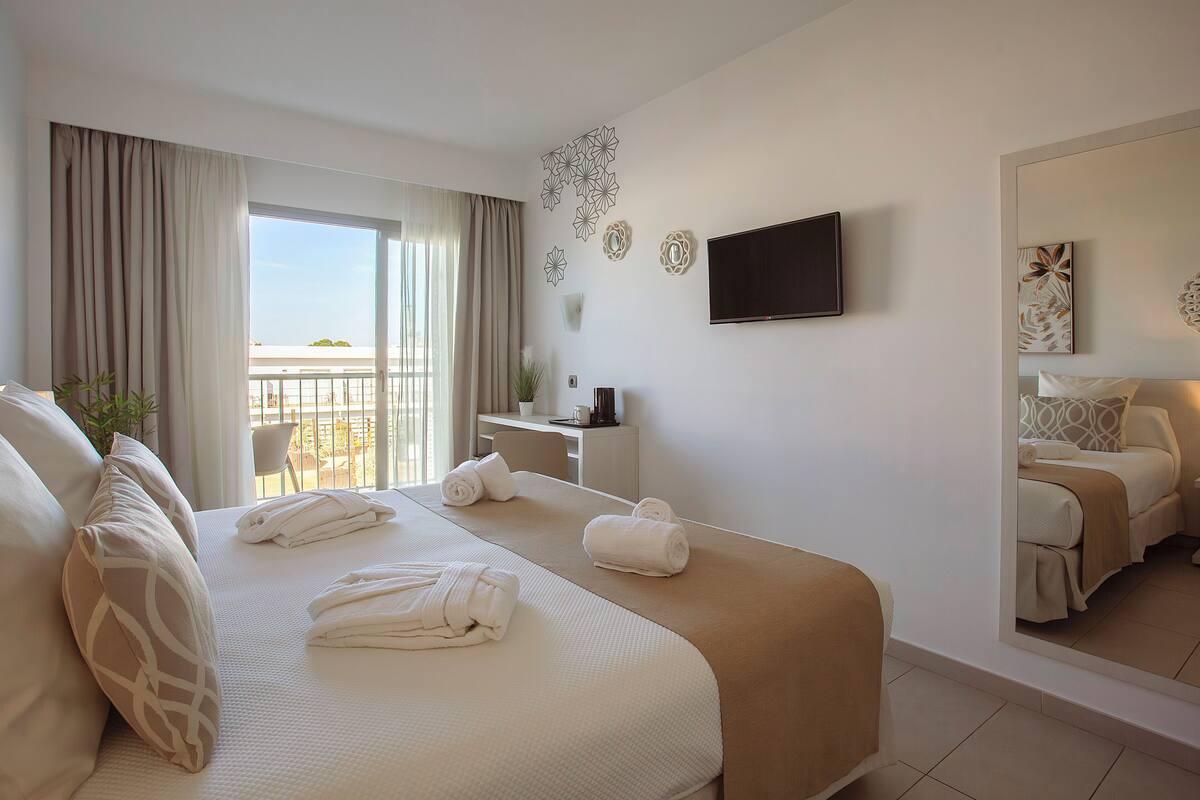 Quarto de hotel com cama, escrivaninha, televisão e varanda com vista.