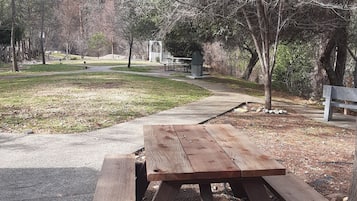 Mesa de piquenique num parque com um caminho pavimentado, bancos e árvores.