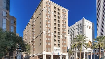 Um hotel de vários andares com uma entrada destacada, uma placa indicando ser um Homewood Suites by Hilton, e um céu azul claro ao fundo.