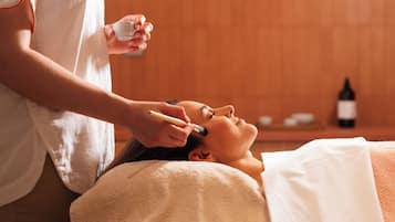 Uma pessoa recebendo tratamento facial em um quarto com painéis de madeira e uma garrafa em uma prateleira.