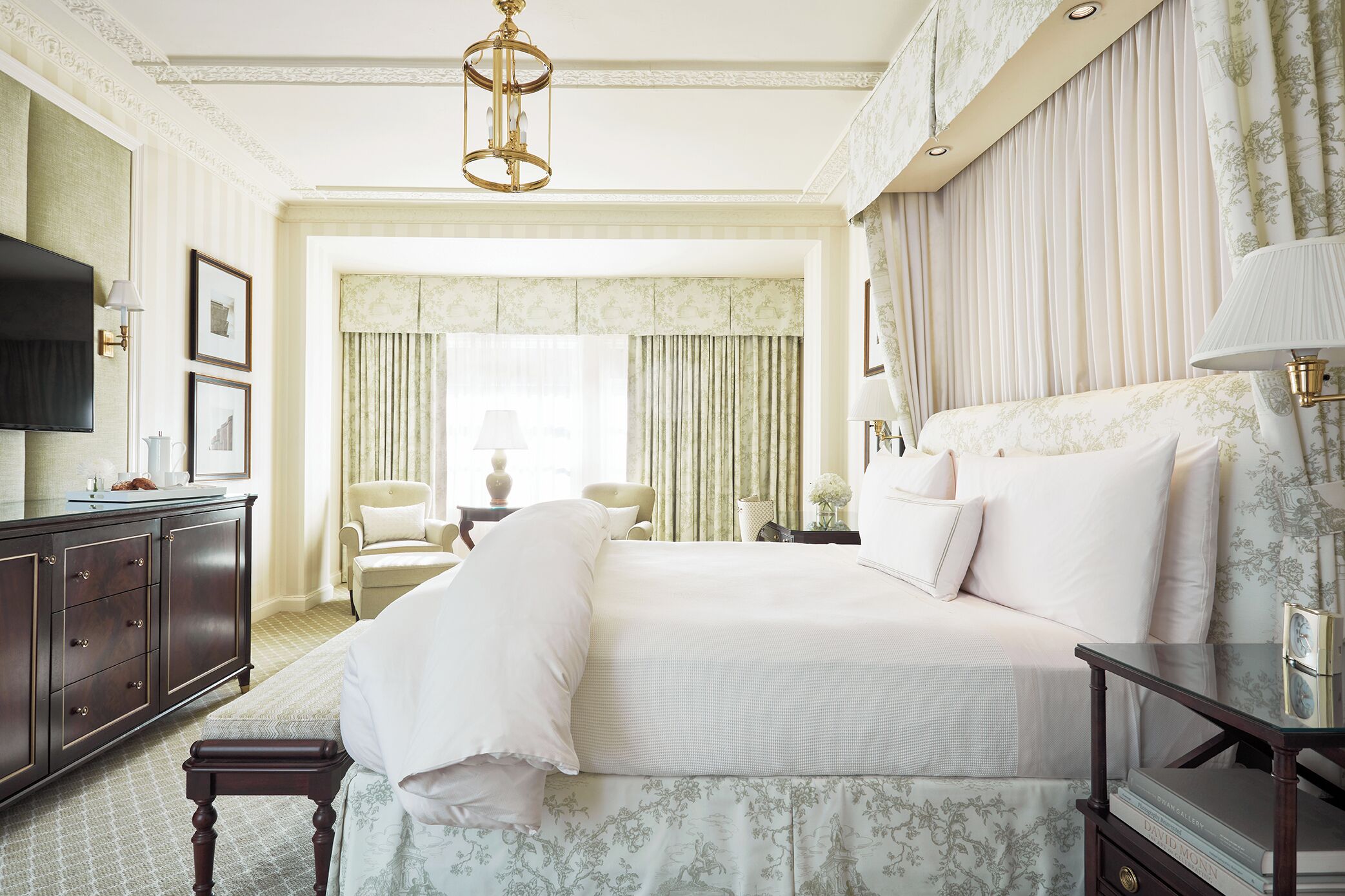 Quarto de hotel com uma cama grande, televisão, escrivaninha e uma cadeira.