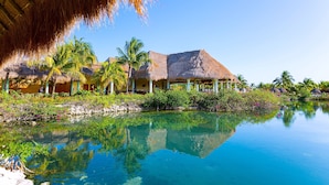 Resort com construções de telhado de palha, piscina cristalina e vegetação exuberante.