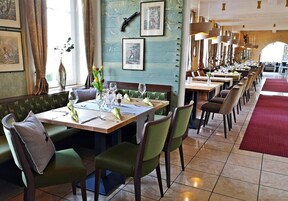 Restaurante com várias mesas, cadeiras estofadas em verde e um tapete vermelho.