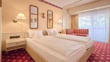 Quarto de hotel com duas camas, um tapete vermelho, uma janela grande com cortinas e luminárias fixadas na parede.