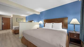 Quarto de hotel com uma cama grande, duas mesas de cabeceira com luminárias, um painel de cabeceira de madeira, uma porta e uma pequena escrivaninha com espelho.
