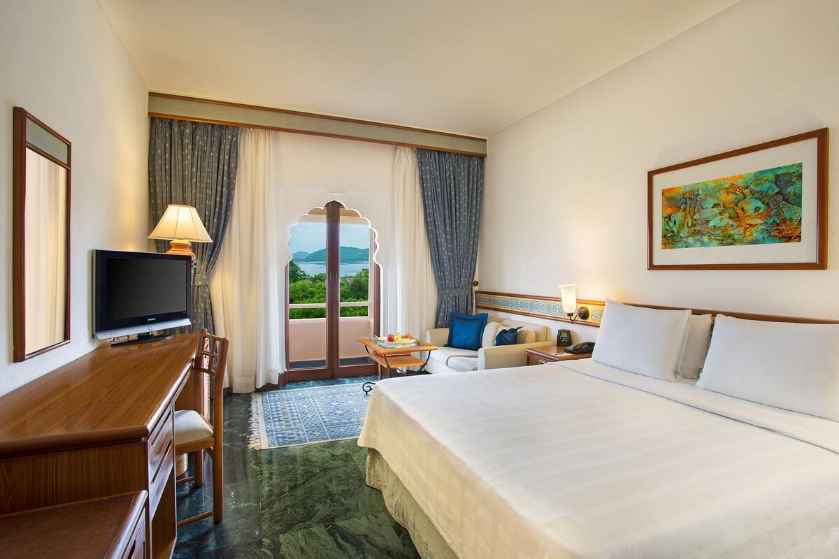 Quarto de hotel com cama, secretária com televisão, sofá e vista para o exterior.