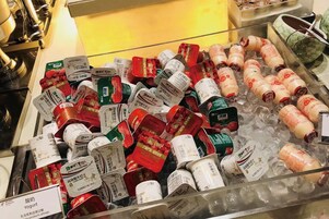 Diversos produtos lácteos embalados, como iogurte e leite, expostos sobre gelo em uma área refrigerada.