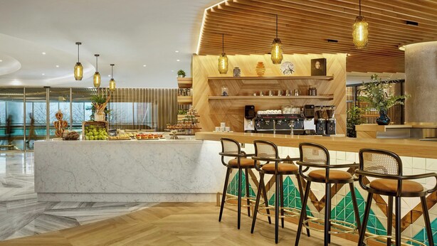 Uma área de bar moderna com bancada de mármore, banquetas de madeira e iluminação pendente.