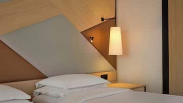 Quarto de hotel moderno com teto inclinado, mesa de cabeceira com luminária e camas bem arrumadas.