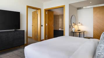 Quarto de hotel com cama, televisão, banheiro e uma pequena mesa com abajur.