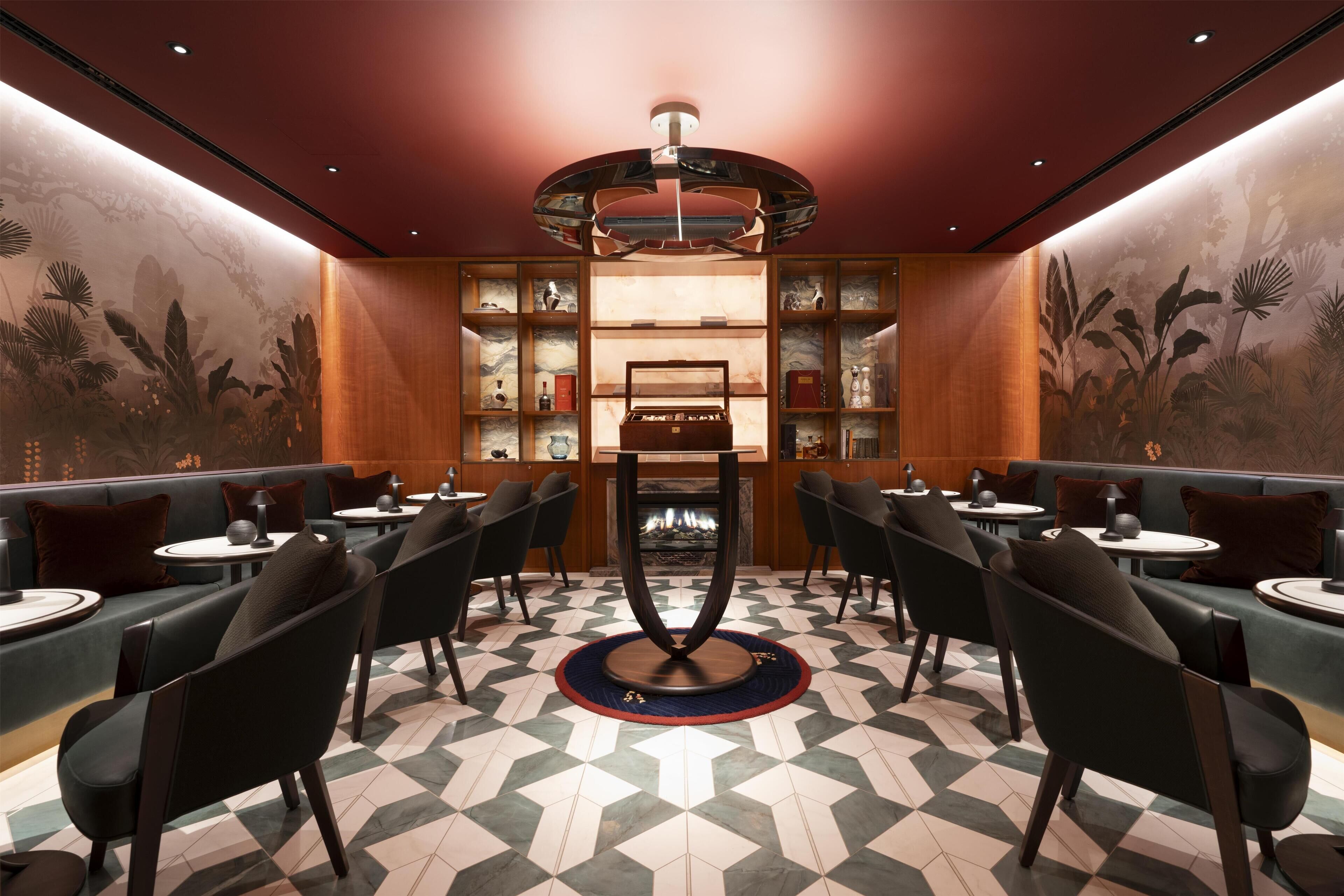 Restaurante com uma mesa redonda central rodeada por cadeiras, piso estampado e prateleiras fixadas na parede com diversos objetos.