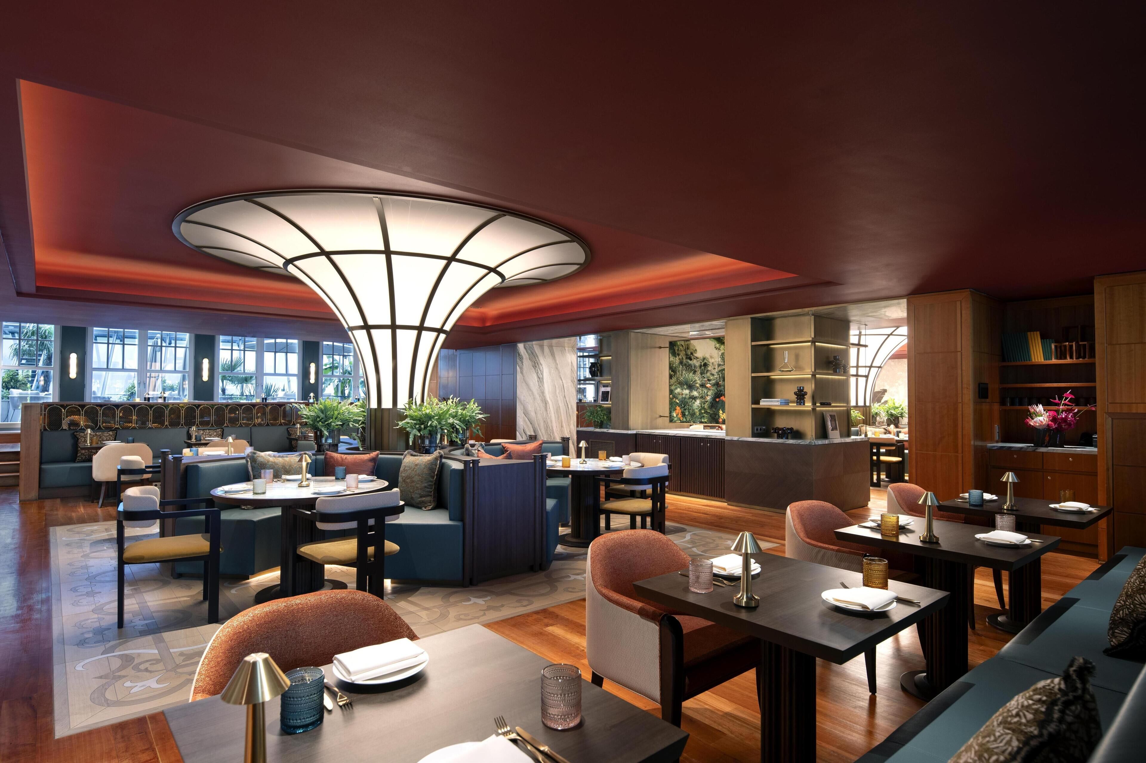 Um restaurante moderno com luminária central, disposição de assentos e vista para o exterior.