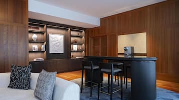 Uma sala de estar moderna com sofá, dois banquetes, uma mesa de centro e um bar embutido com prateleiras e geladeira.