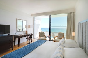 Quarto de hotel com cama grande, escrivaninha, cadeira, televisão e vista para o oceano.