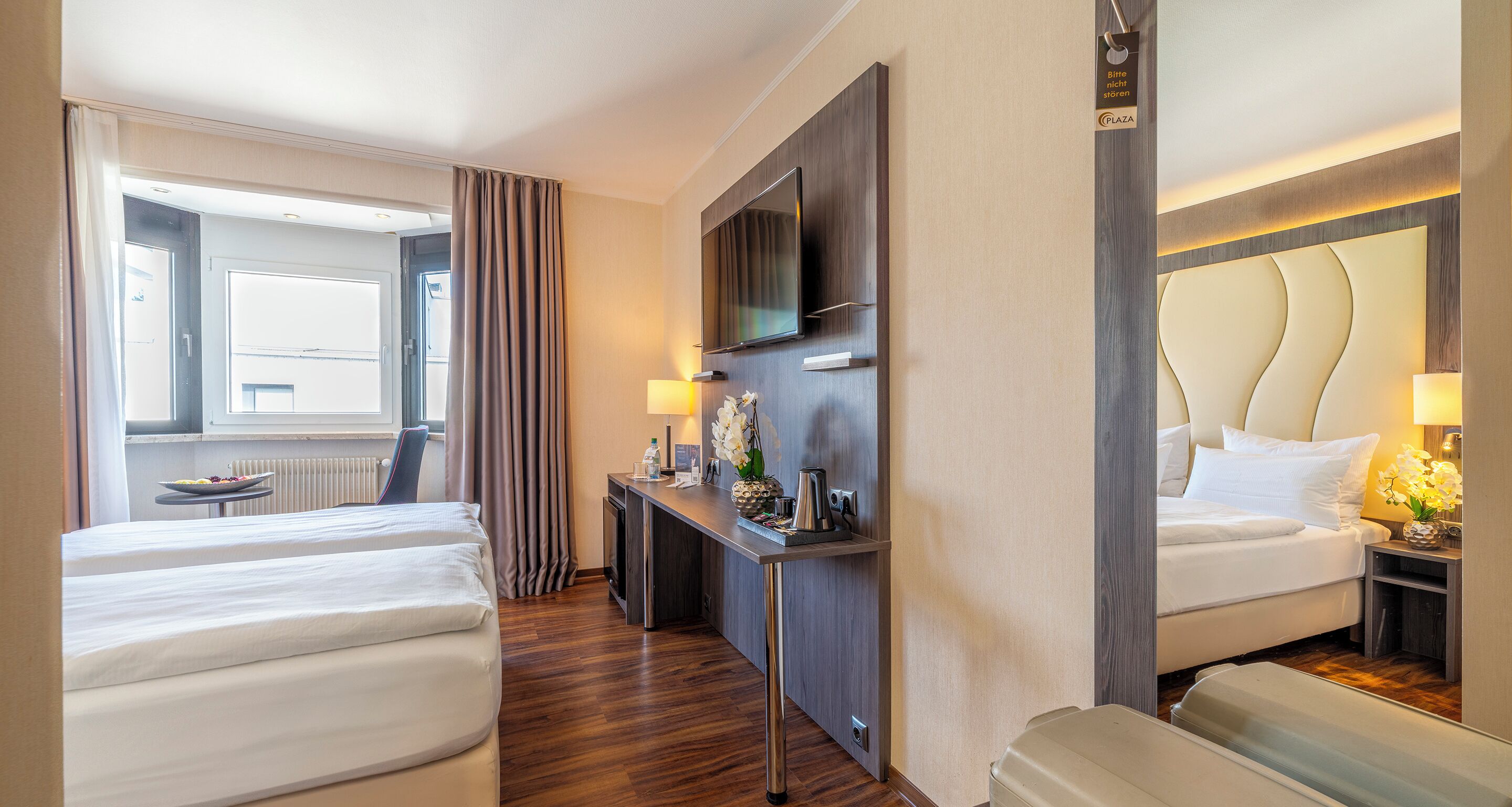 Quarto de hotel com duas camas, uma escrivaninha, uma televisão e vista para o exterior.