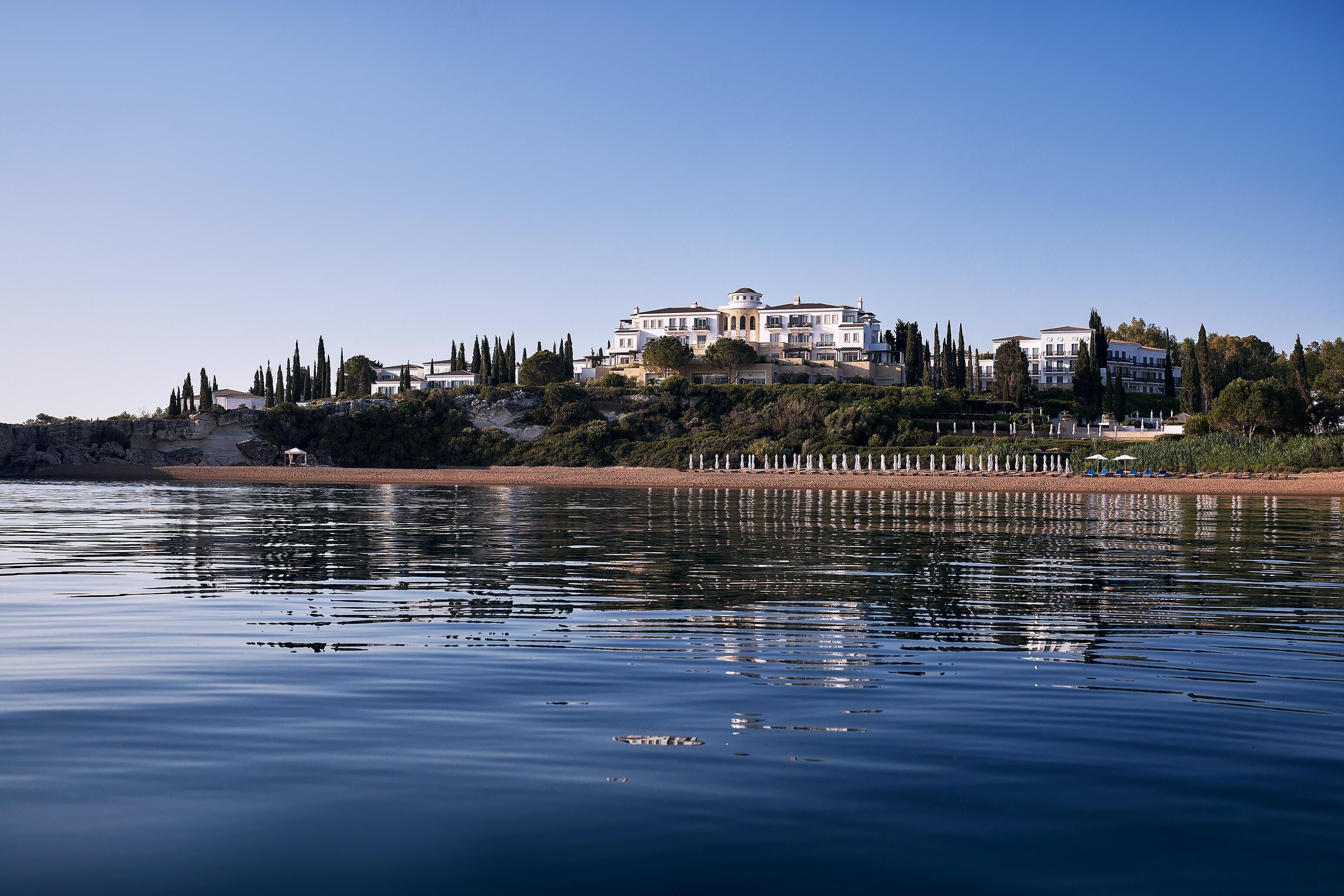 Um edifício grande, com vários andares e fachada branca, localizado numa encosta com vista para águas calmas.