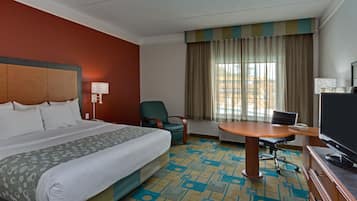 Quarto de hotel com uma cama grande, uma escrivaninha com televisão, uma cadeira e uma janela com cortinas.