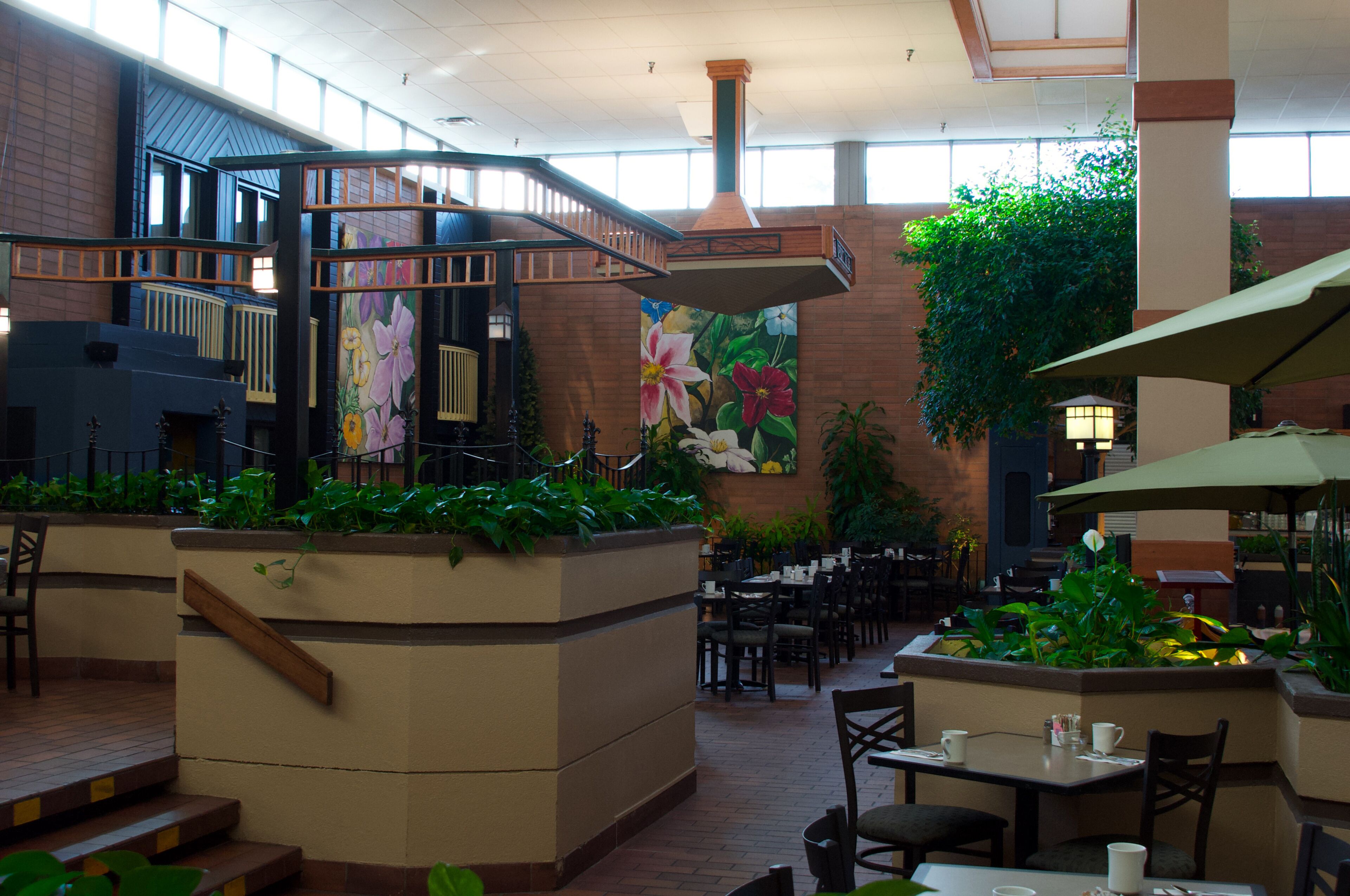 Amplo espaço interno com várias mesas e cadeiras para refeições, uma escada e um grande mural de flores na parede.
