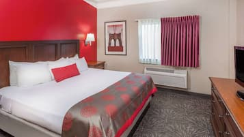 Quarto de hotel com cama grande, mesa de cabeceira com luminária, quadro pendurado na parede, janela com cortinas e televisão em cômoda de madeira.