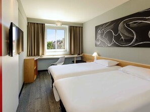 Quarto de hotel com duas camas, uma escrivaninha, uma cadeira, uma televisão e uma janela com cortinas.