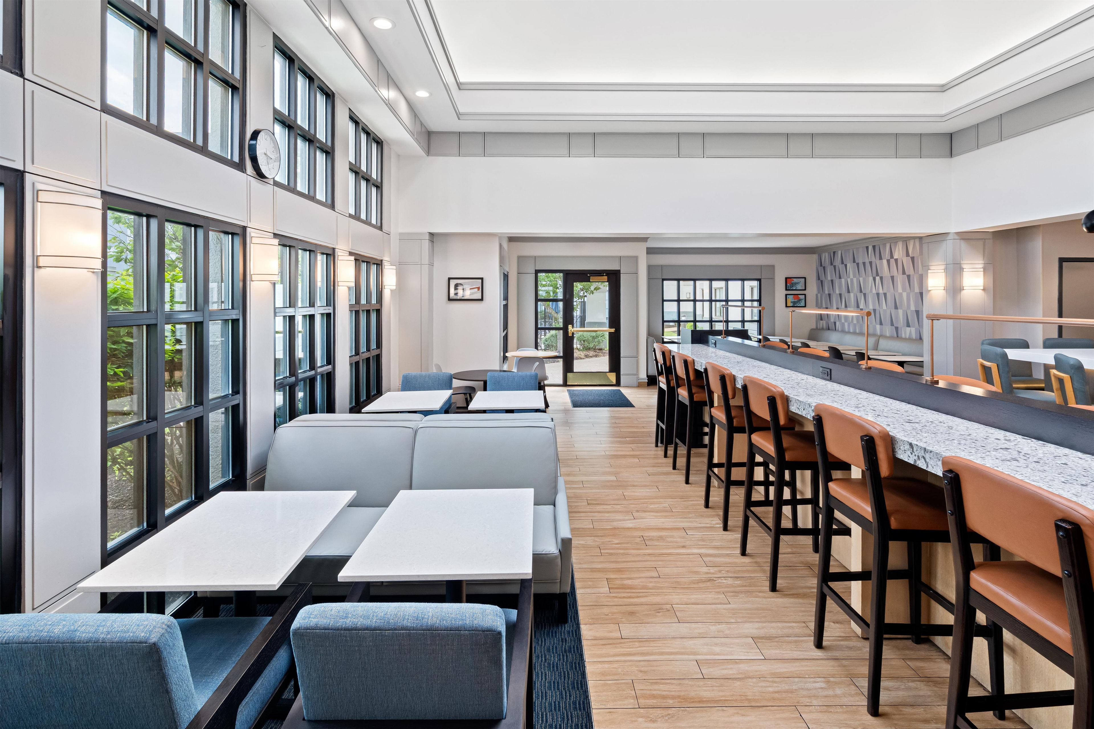 Um restaurante moderno com pé-direito alto, grandes janelas e um balcão comprido com banquetas.