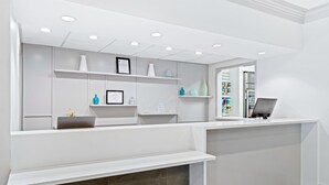 Uma receção com balcão branco, prateleiras com objetos decorativos e um certificado emoldurado.